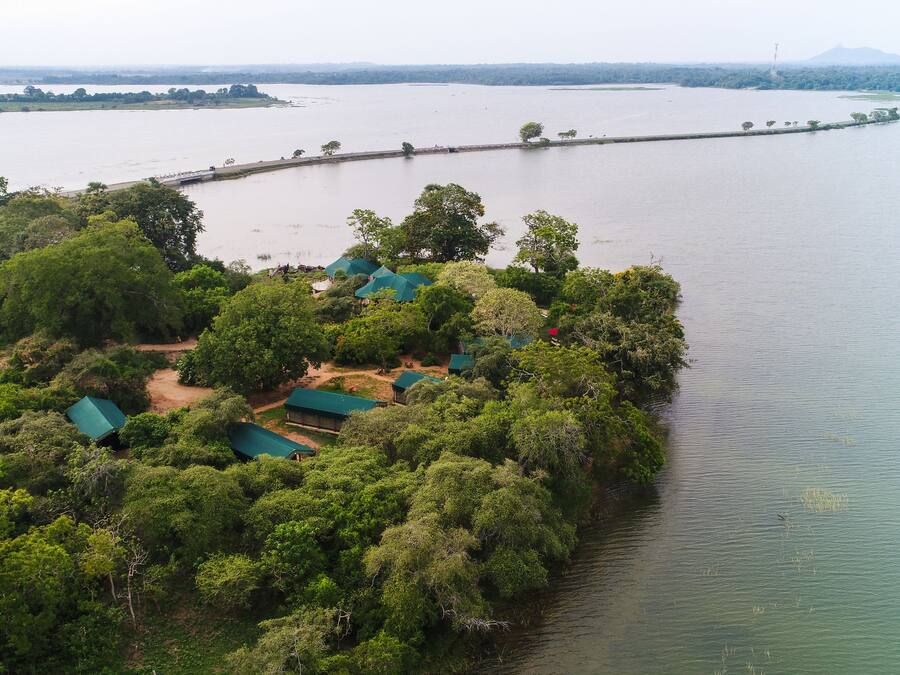 Vista aérea de uma propriedade à beira de um lago, com várias cabanas de telhado verde, rodeadas por vegetação densa.