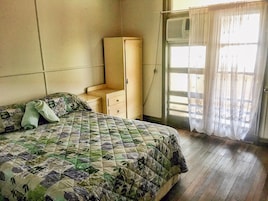 Quarto com cama, mesa de cabeceira, guarda-roupa e janela com cortinas.