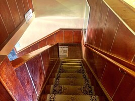 Uma escada de madeira com carpete estampado, um aviso de cuidado e um corrimão.