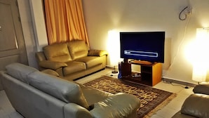 Uma sala de estar com sofá, poltrona e televisão sobre um suporte.