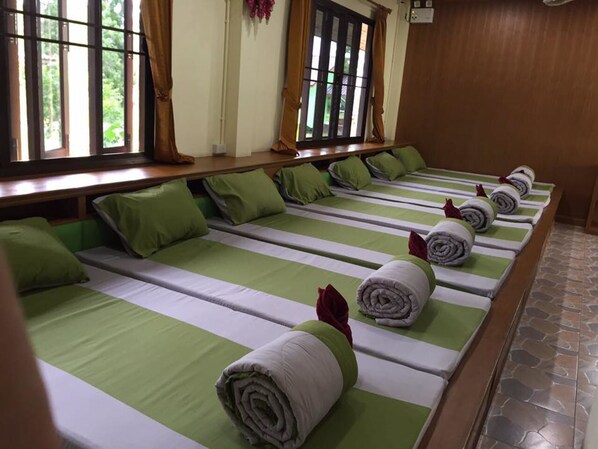 Uma fileira de camas de solteiro com roupa de cama verde e branca listrada, bem arrumada com toalhas enroladas e almofadas.