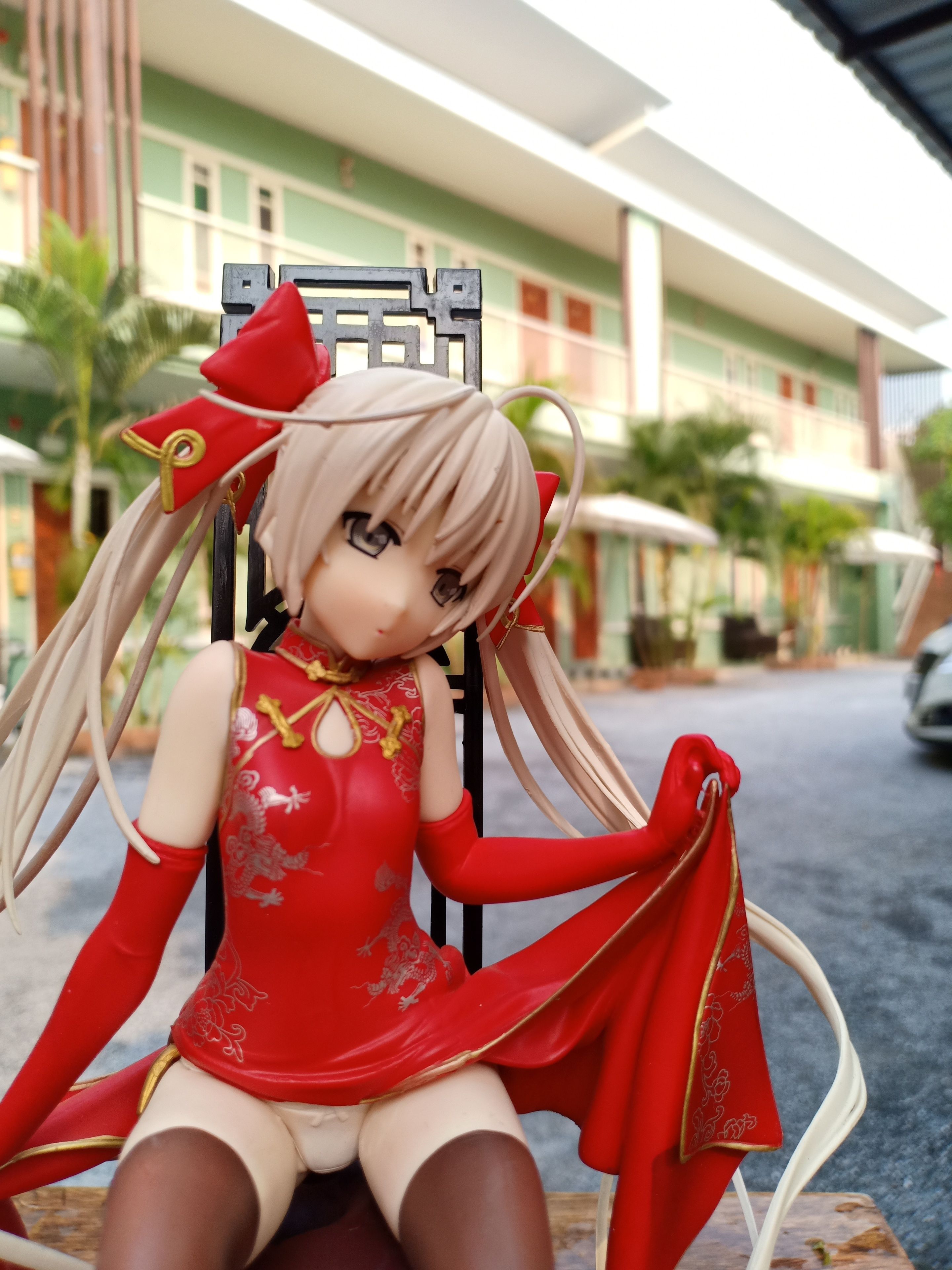 Uma figura de um personagem vestido de vermelho com detalhes dourados, sentado em uma cadeira com uma placa acima.