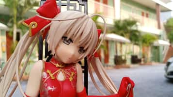 Uma figura de um personagem vestido de vermelho com detalhes dourados, sentado em uma cadeira com uma placa acima.