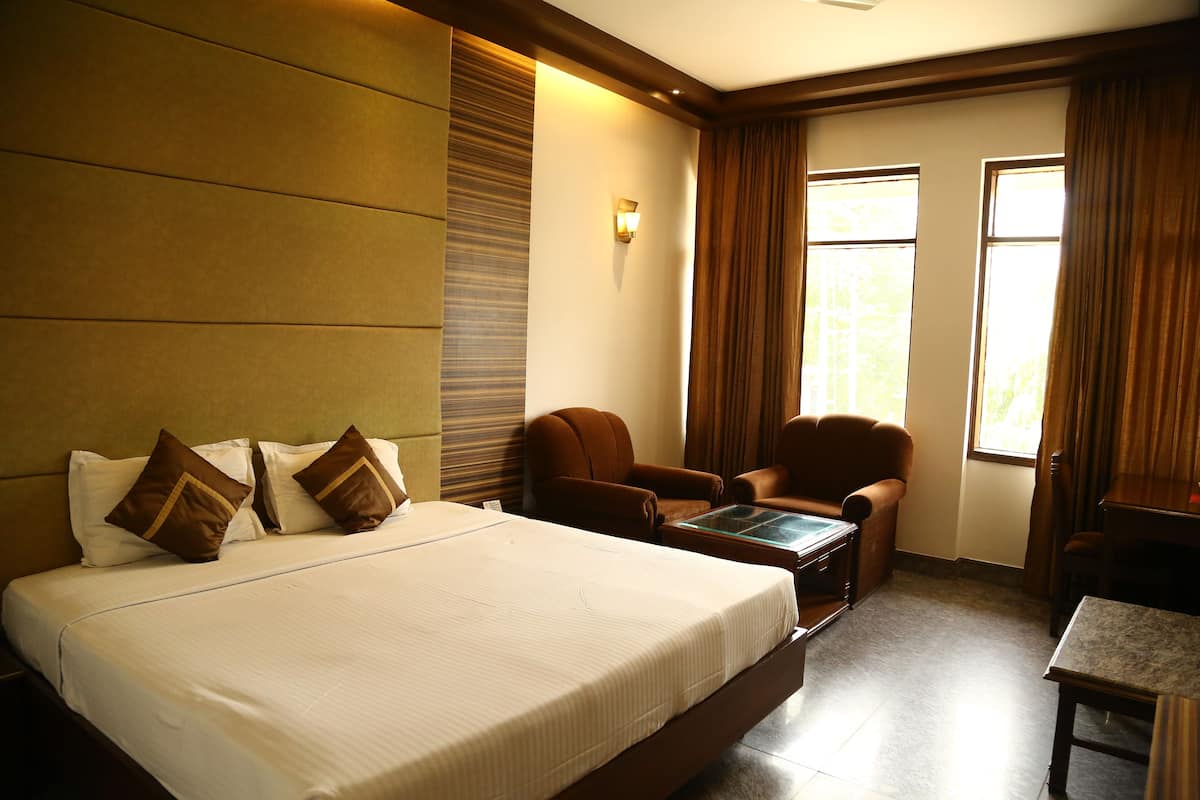 Quarto de hotel com uma cama grande, duas poltronas, uma mesinha e uma janela com cortinas.