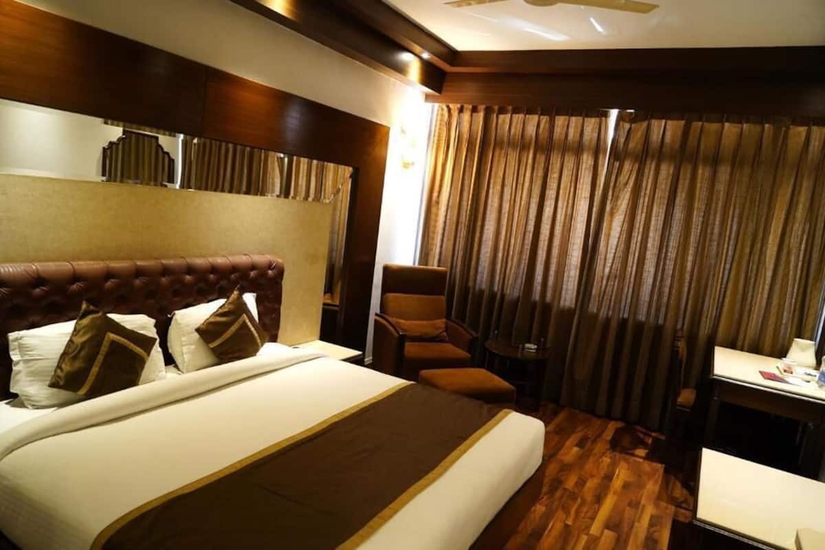 Quarto de hotel com uma cama grande, uma escrivaninha, uma cadeira e uma cortina.