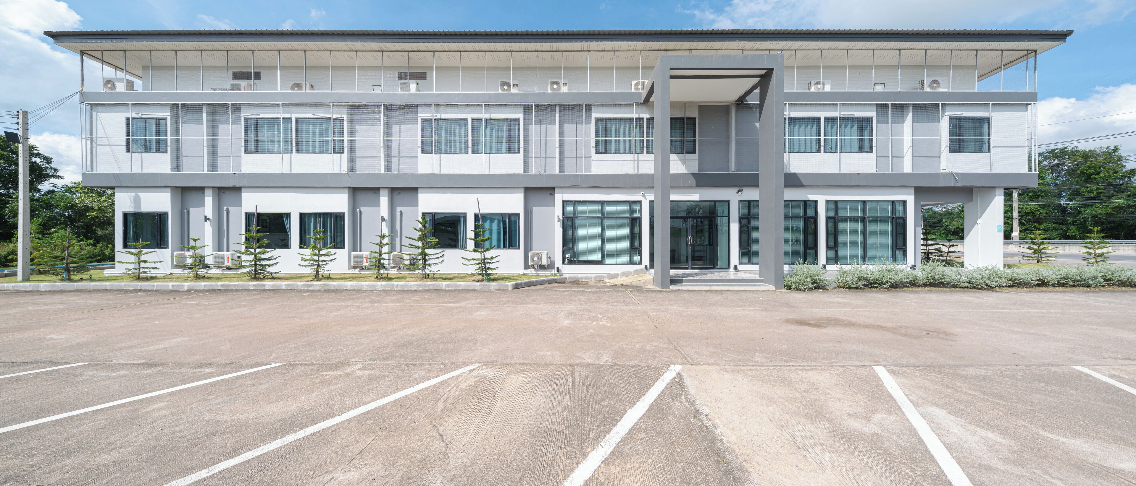 Um edifício moderno com telhado plano, janelas amplas e um estacionamento à frente.