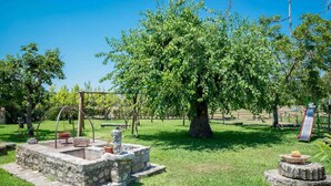 Uma fonte de pedra com arco de metal, cercada por grama e árvores em um parque.