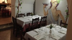 Restaurante com toalhas de mesa brancas, cadeiras de madeira e um mural de um homem segurando uma taça de vinho.