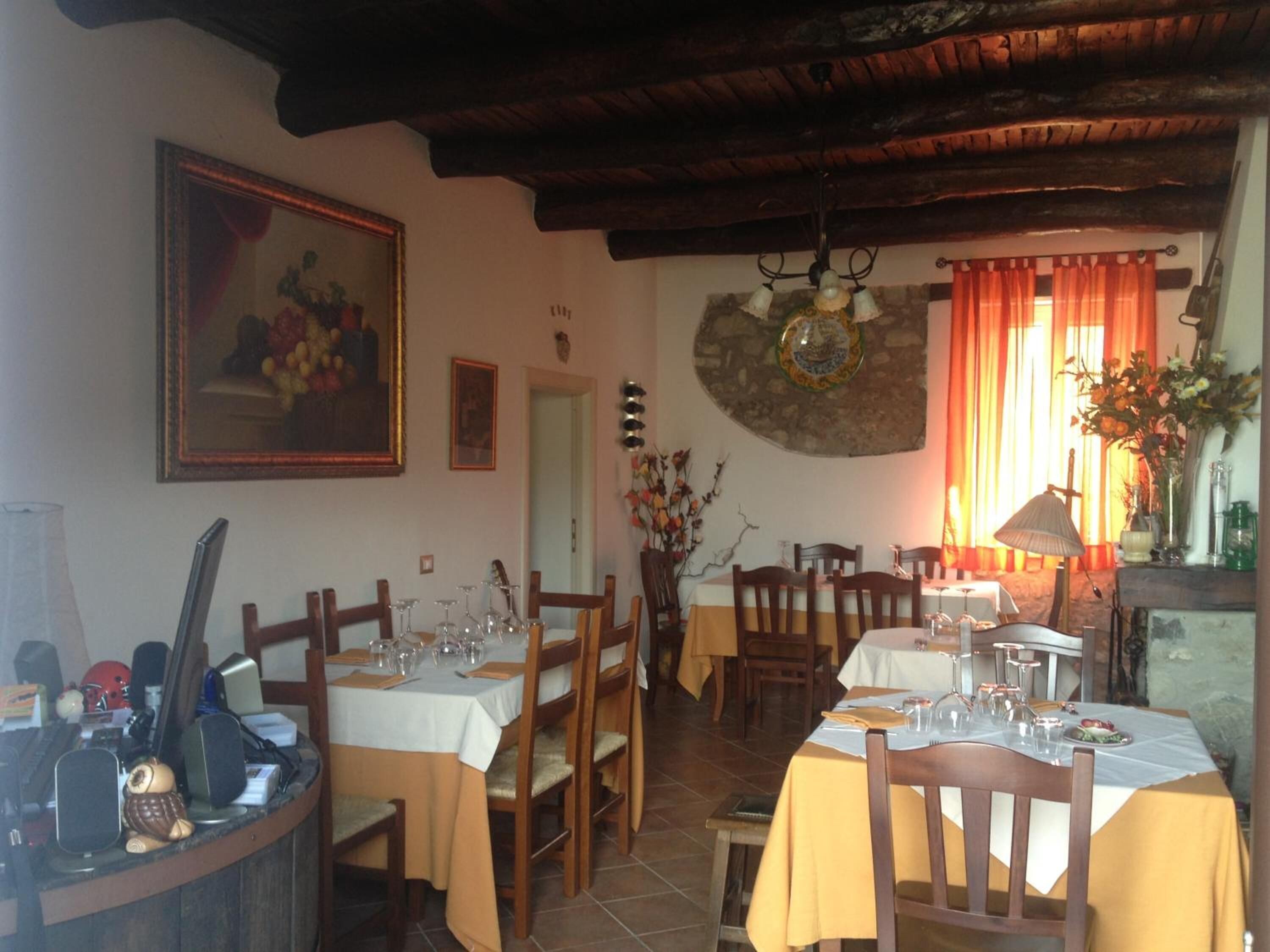 Uma sala de jantar com mesas preparadas para dois, cadeiras de madeira, um candelabro e um quadro na parede.