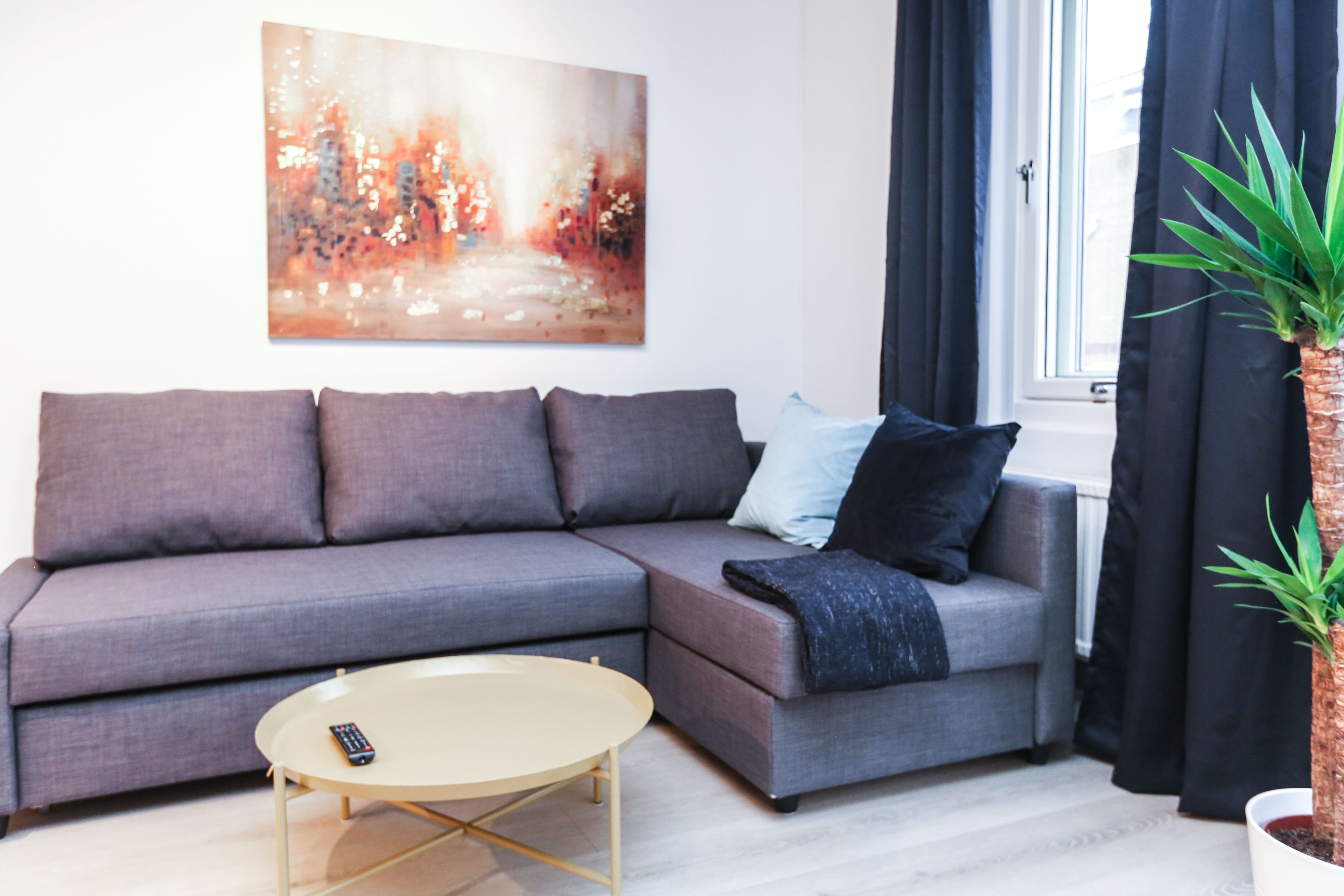 Uma sala de estar moderna com um sofá seccional cinza, uma mesa de centro redonda, um quadro na parede e uma planta em vaso.