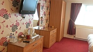 Quarto de hotel com televisão na parede, guarda-roupa de madeira, secretária com espelho e uma cama.