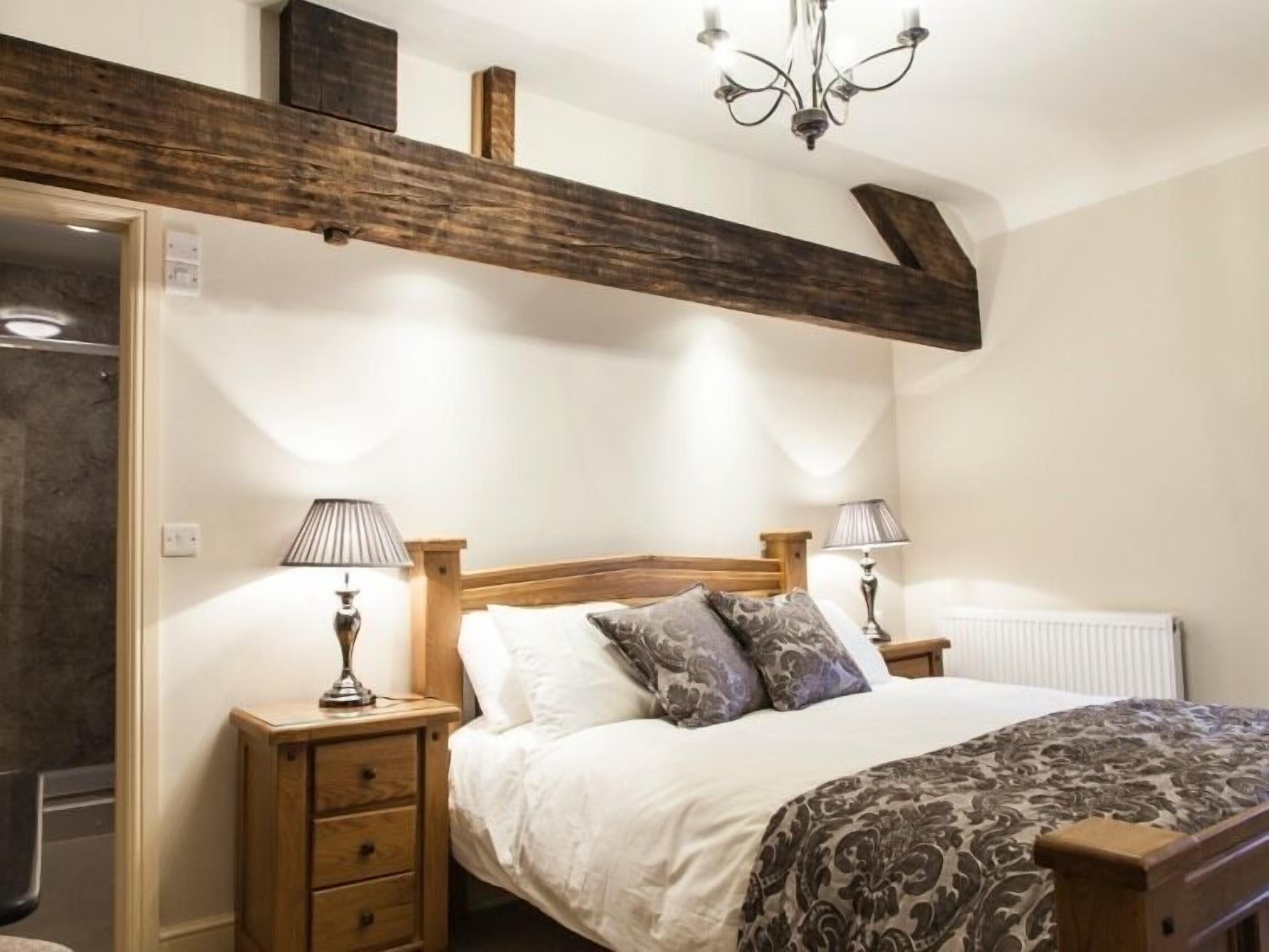 Quarto com cabeceira de madeira, duas mesas de cabeceira com luminárias, cama com roupa de cama estampada e um candelabro.