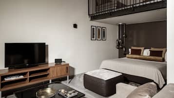 Uma sala de estar moderna com televisão de tela plana, móvel para aparelhos de som de madeira e uma cama grande com muitos travesseiros.