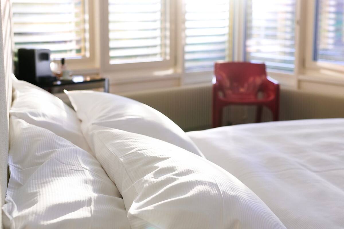 Quarto de hotel com cama, almofadas, escrivaninha e cadeira.
