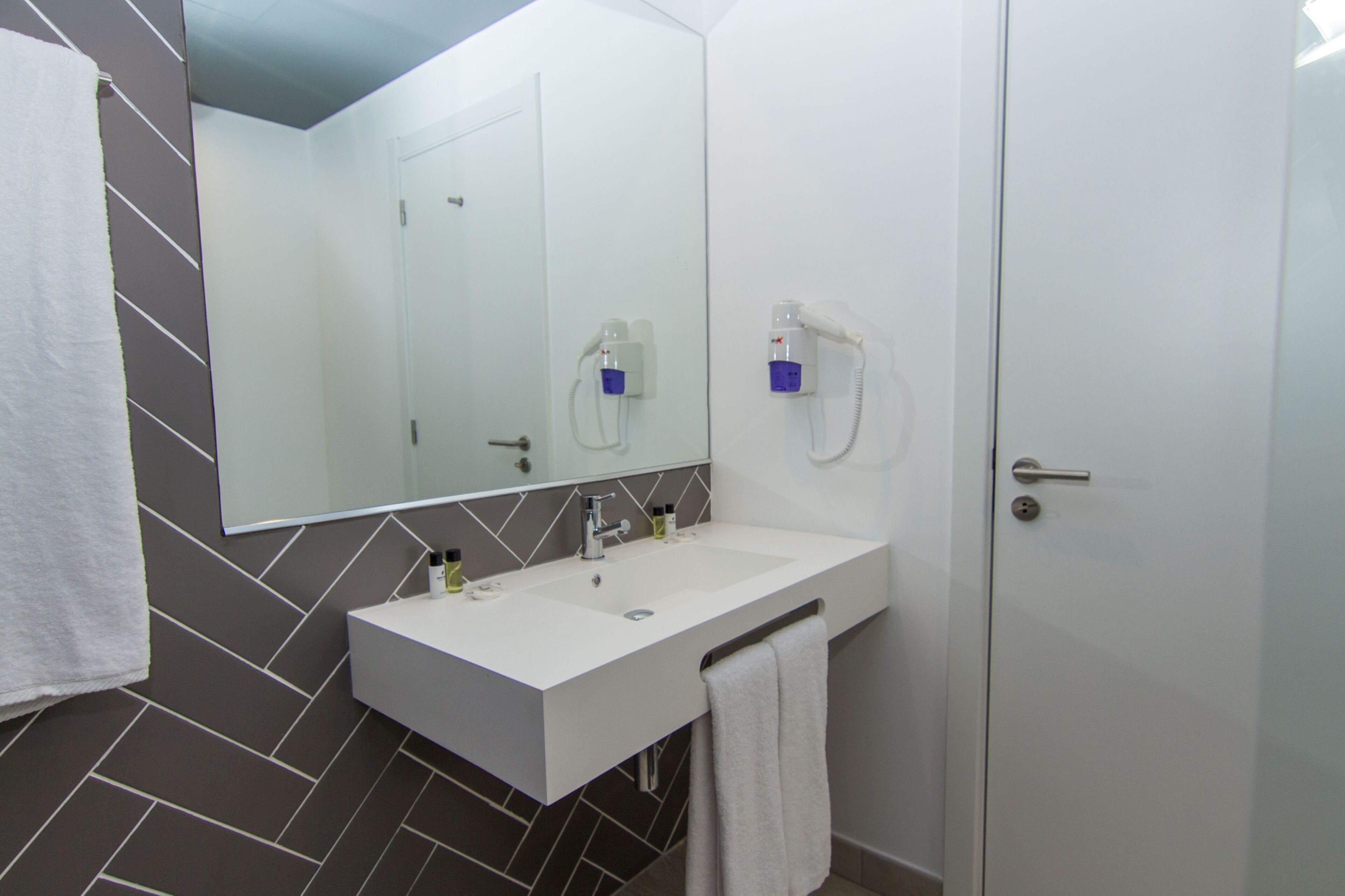 Casa de banho com lavatório branco, espelho e suporte para toalhas.
