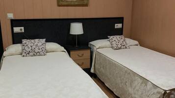 Quarto de hotel com duas camas de solteiro, uma mesinha de cabeceira com abajur, um quadro na parede e painéis de madeira.