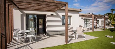 Um pátio moderno ao ar livre com pérgola, móveis brancos e gramado bem cuidado.