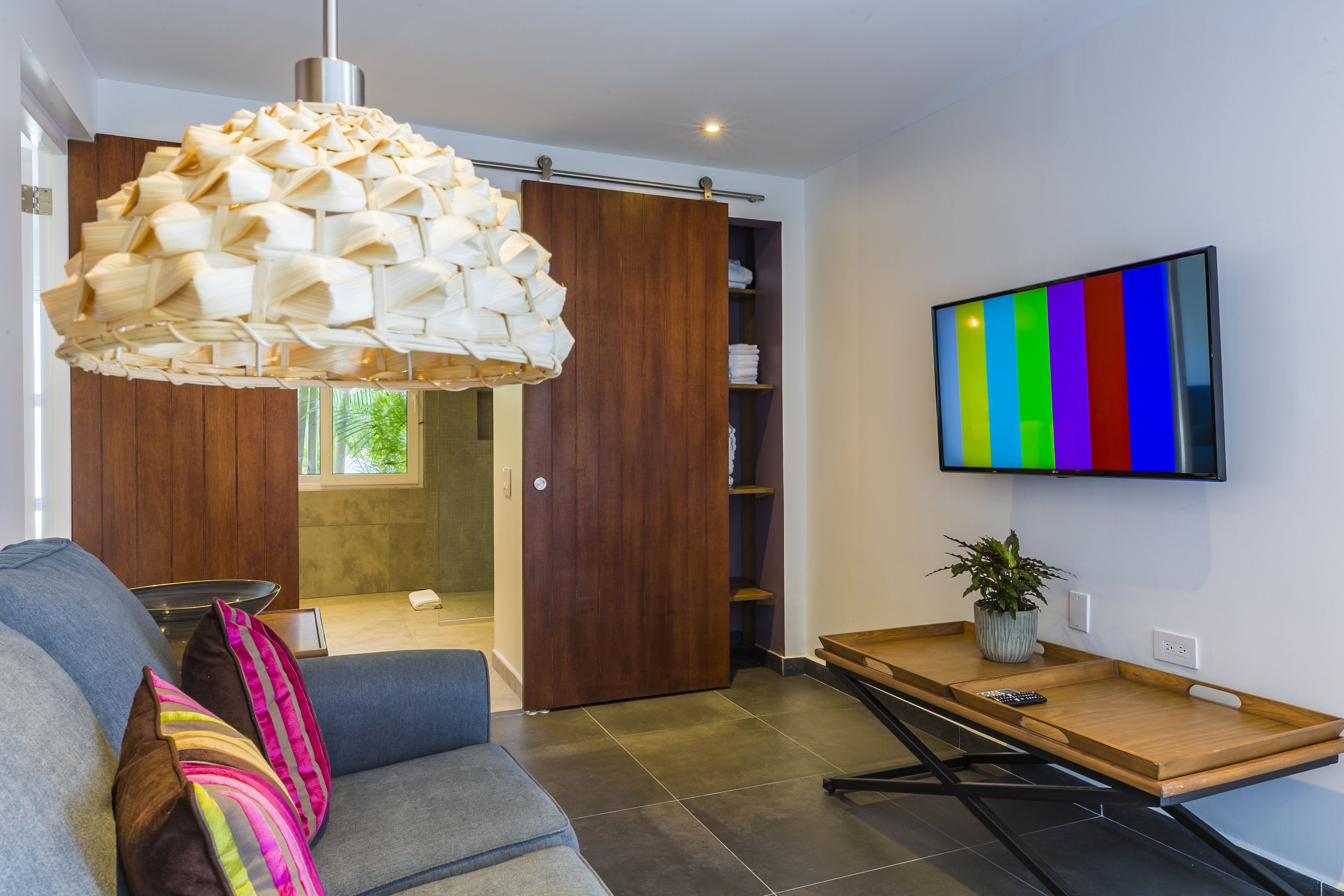 Uma sala de estar moderna com um sofá cinza, uma luminária pendente diferenciada, uma mesa de centro de madeira e uma TV de tela plana na parede.