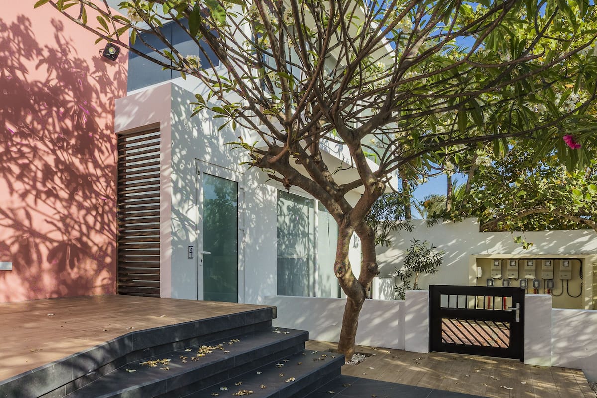 Um edifício moderno com uma escadaria que leva a uma porta, rodeado por árvores e um céu claro.