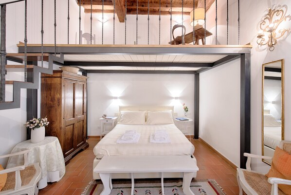 Quarto com uma cama grande, duas mesas de cabeceira, um guarda-roupa de madeira, um banco e uma pequena mesa com um vaso de flores.