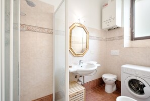 Casa de banho com chuveiro, lavatório, sanita e máquina de lavar roupa.