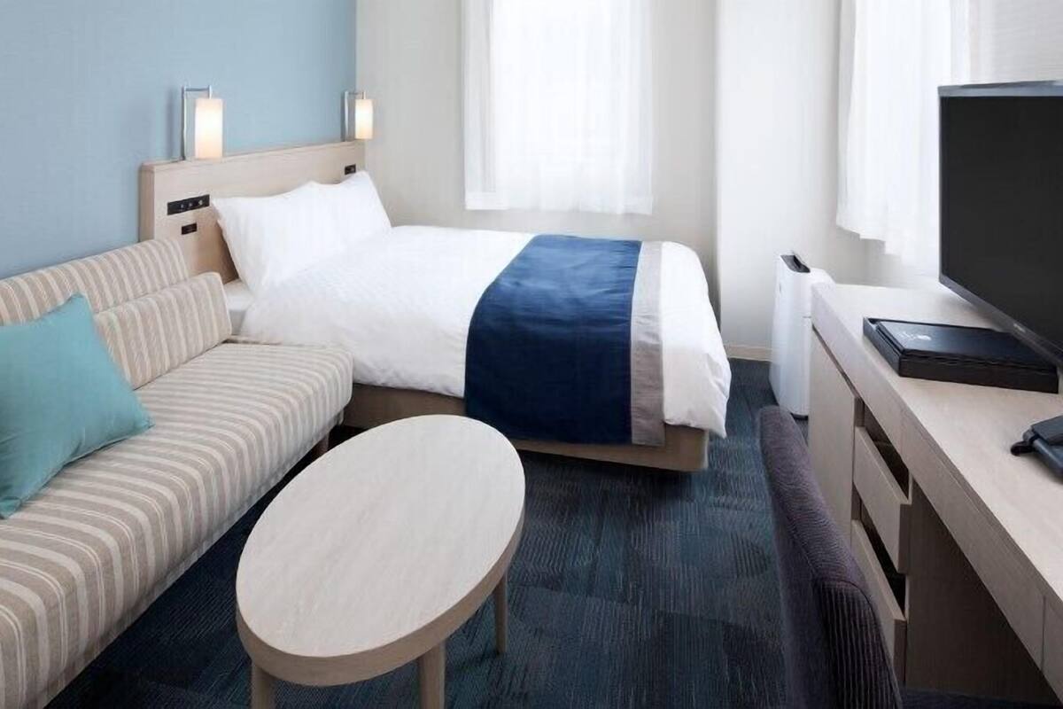Quarto de hotel com cama, sofá, mesinha, televisão e escrivaninha.