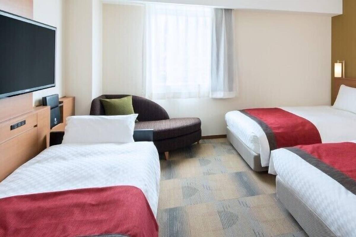 Quarto de hotel com duas camas, televisão, escrivaninha e janela.
