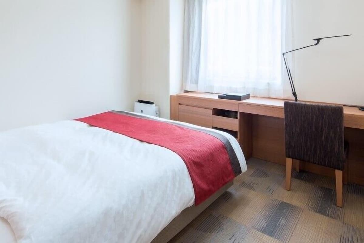 Quarto de hotel com cama, escrivaninha e uma cadeira.