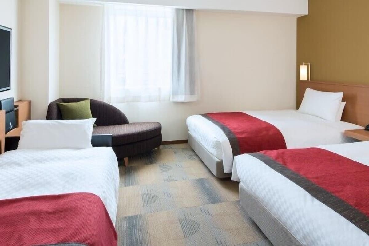 Quarto de hotel com duas camas, um sofá, uma televisão e uma janela com cortinas.