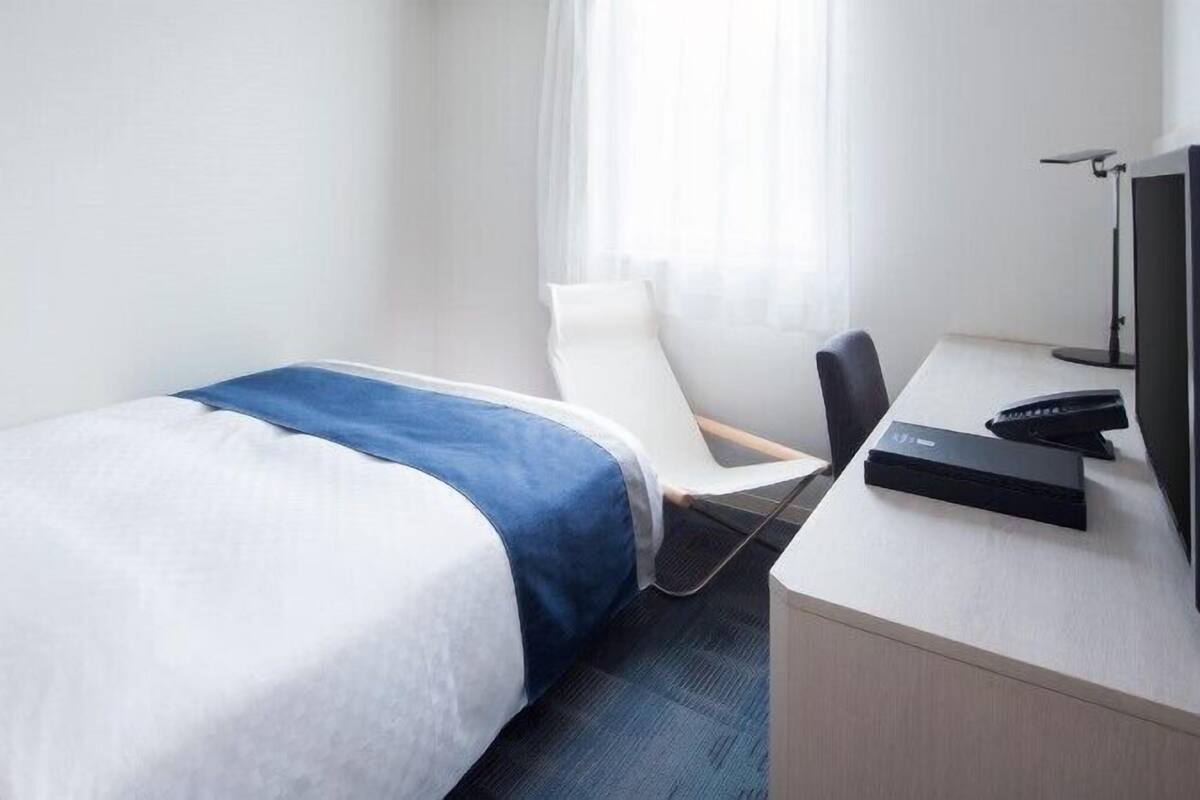 Quarto de hotel com uma cama, uma escrivaninha com computador e uma cadeira.