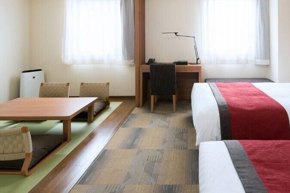 Quarto de hotel com cama, escrivaninha, cadeira, mesa e luminária.