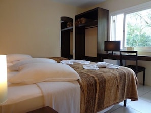 Quarto de hotel com cama, escrivaninha e televisão.