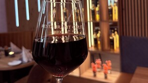 Um copo de vinho tinto num restaurante com decoração em madeira e um bar ao fundo.