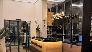 Uma área de recepção de hotel moderna, com um balcão de madeira, portas de vidro que dão para uma sala de jantar e um bar com vitrine de vidro.