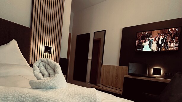 Quarto de hotel com cama bem arrumada, televisão em suporte de madeira e espelho fixado na parede.