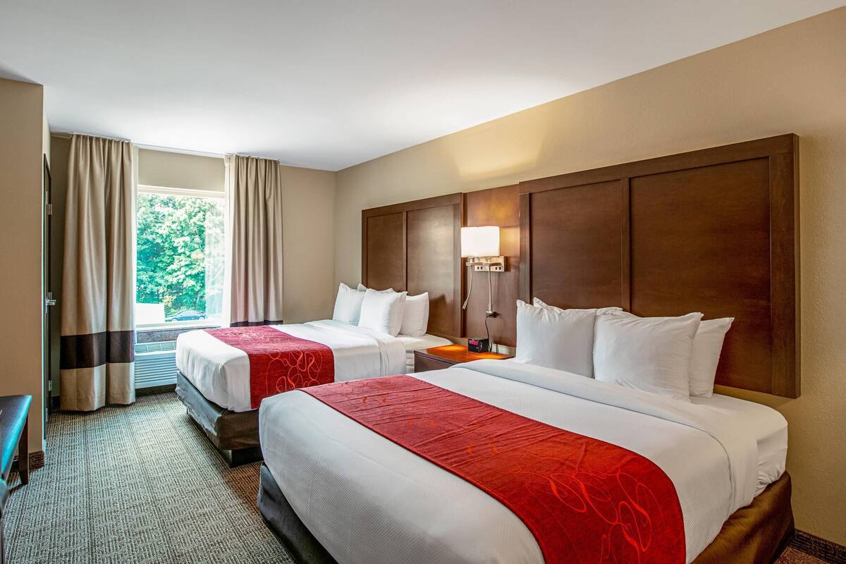 Quarto de hotel com duas camas, uma mesa de trabalho e uma janela com cortinas.