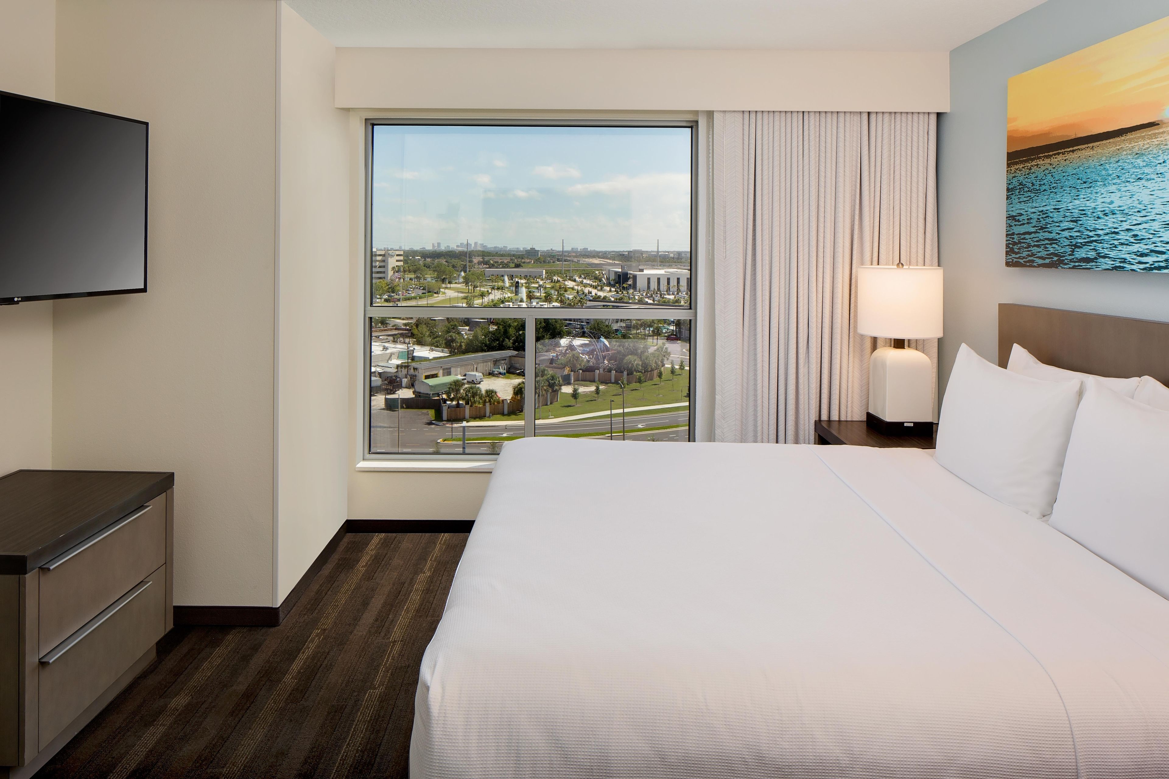 Quarto de hotel com cama grande, televisão de tela plana, janela com vista para a cidade e um quadro na parede.