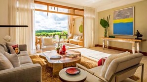 Uma sala de estar espaçosa com uma janela grande, uma mesa de centro, sofás e um quadro na parede.
