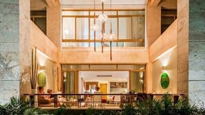 Um hall de hotel moderno com átrio central, janelas amplas e área de estar com vista para o interior.
