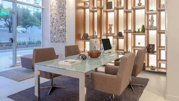 Escritório moderno com mesa de vidro, cadeiras bege e parede decorativa com prateleiras.