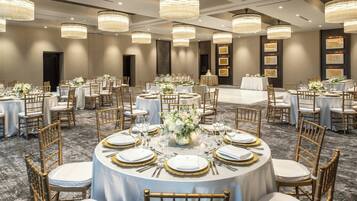 Uma sala de banquetes com mesas redondas, cadeiras douradas e lustres.