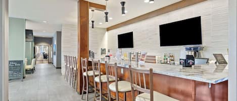 Uma área de bar moderna com um balcão comprido, vários bancos altos e iluminação pendente.