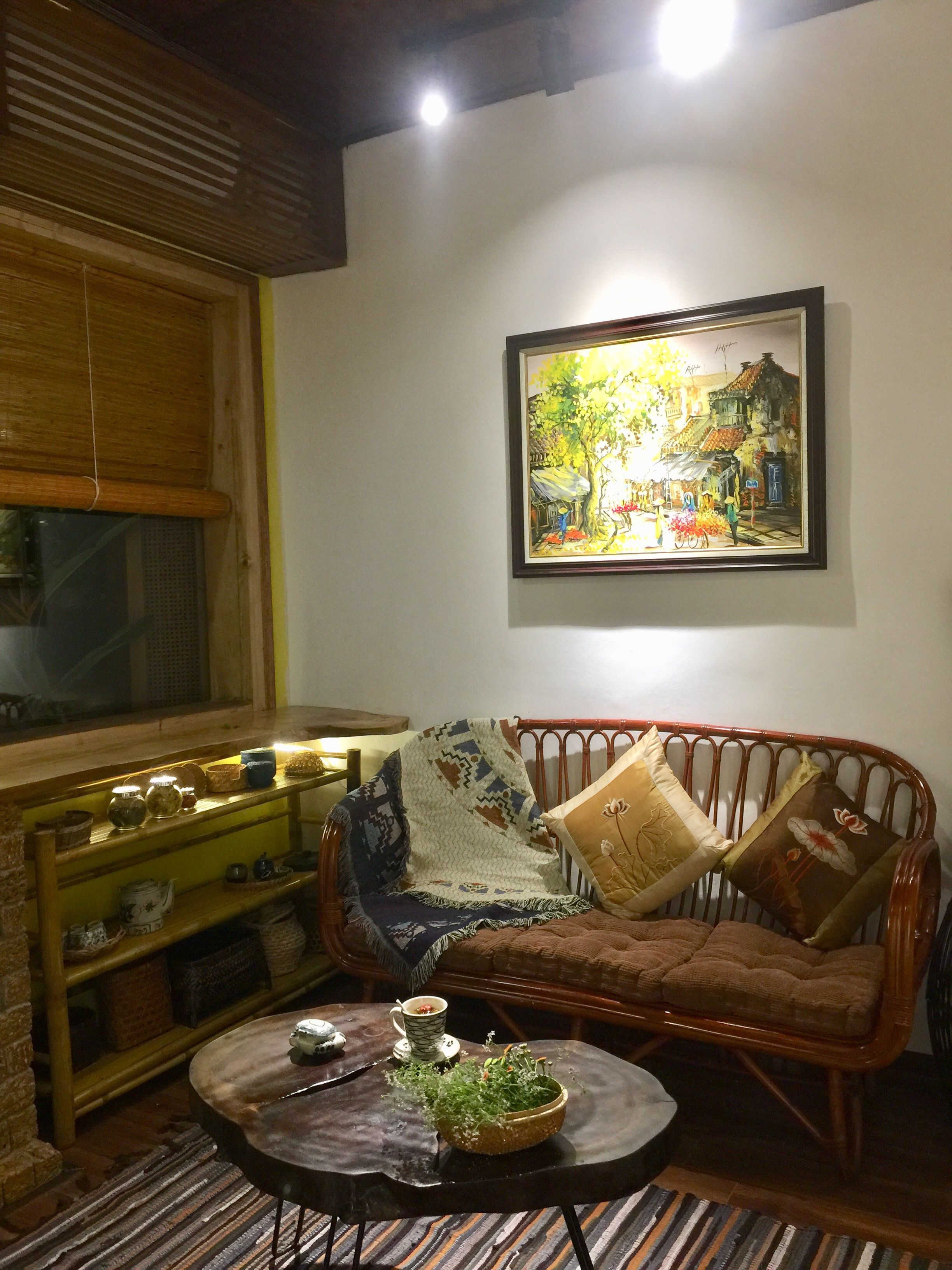 Uma sala de estar aconchegante com um sofá de madeira, uma pequena mesa redonda com uma planta e uma estante com objetos decorativos.