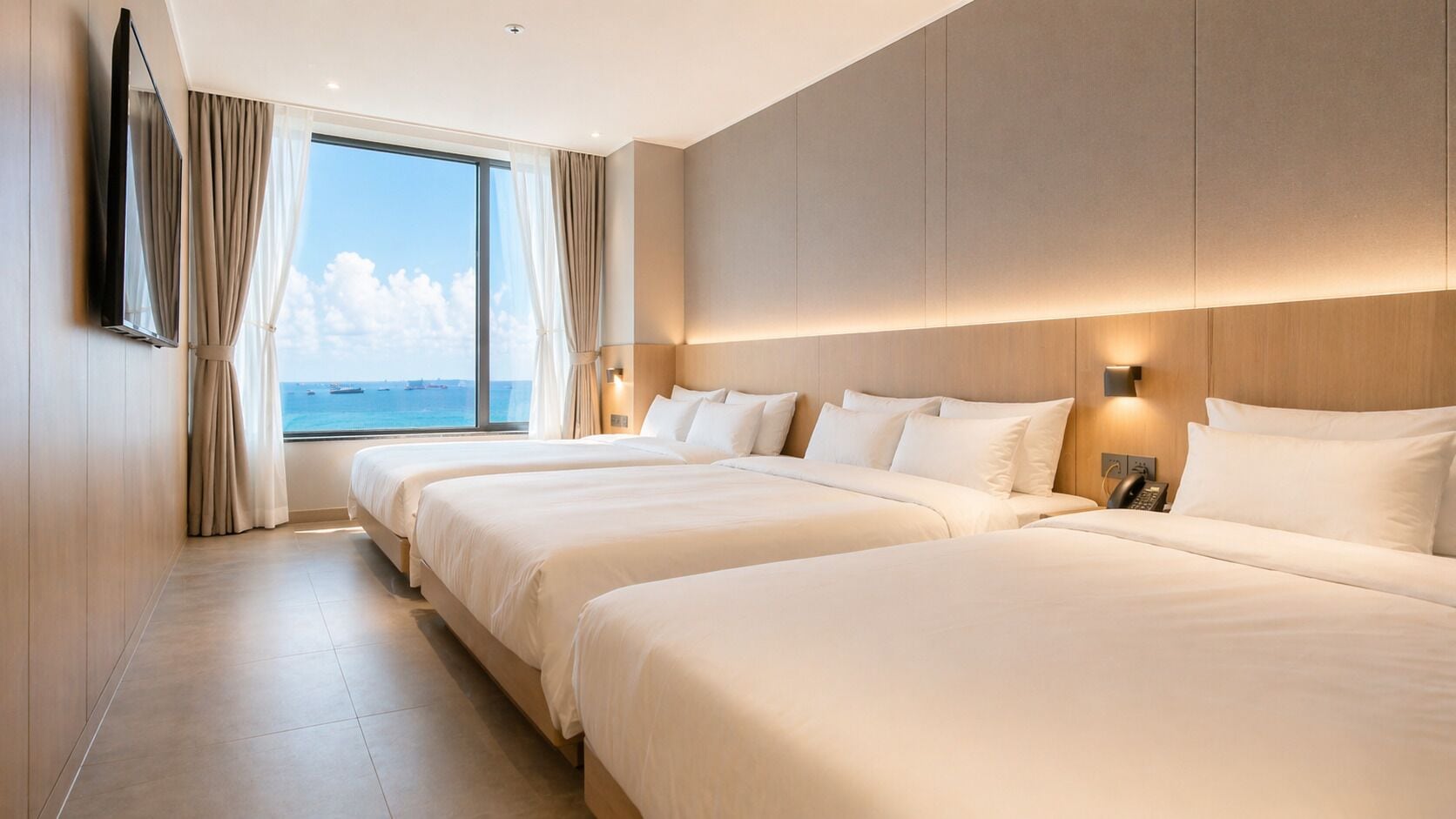 Quarto de hotel com duas camas, televisão, telefone e vista para o mar.