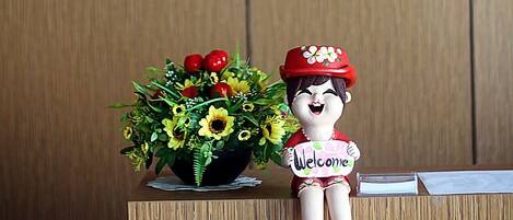 Bancada de recepção com uma placa decorativa de boas-vindas, um arranjo floral e um lustre.