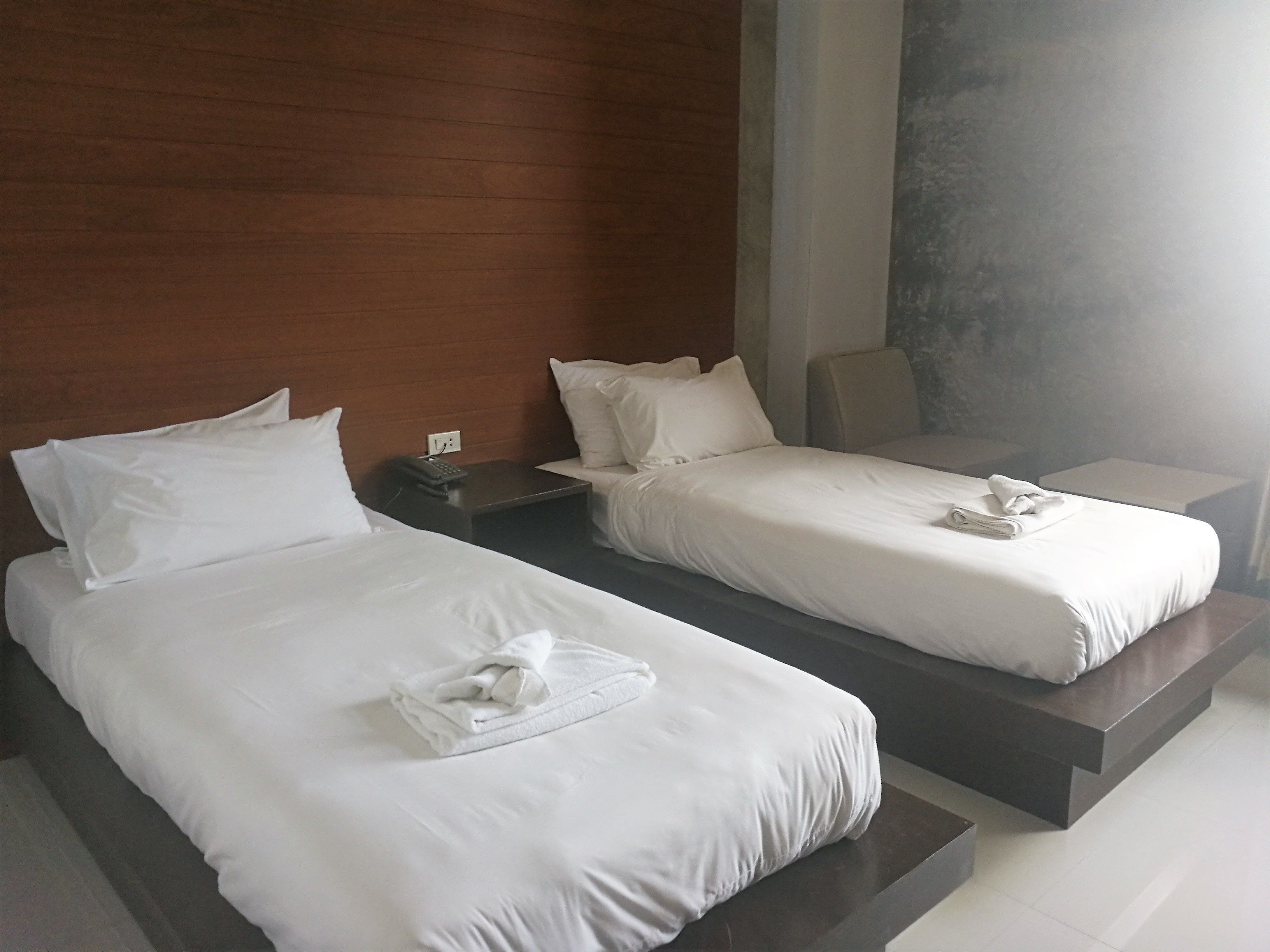 Quarto de hotel com duas camas, uma mesa de cabeceira e uma cadeira.
