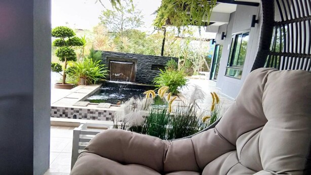 Uma área de estar moderna ao ar livre, com vista para um jardim ajardinado e um espelho d'água.