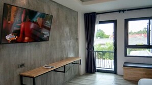 Quarto de hotel moderno com uma televisão grande fixada na parede, um banco de madeira, uma varanda com vista e uma cama com cabeceira.