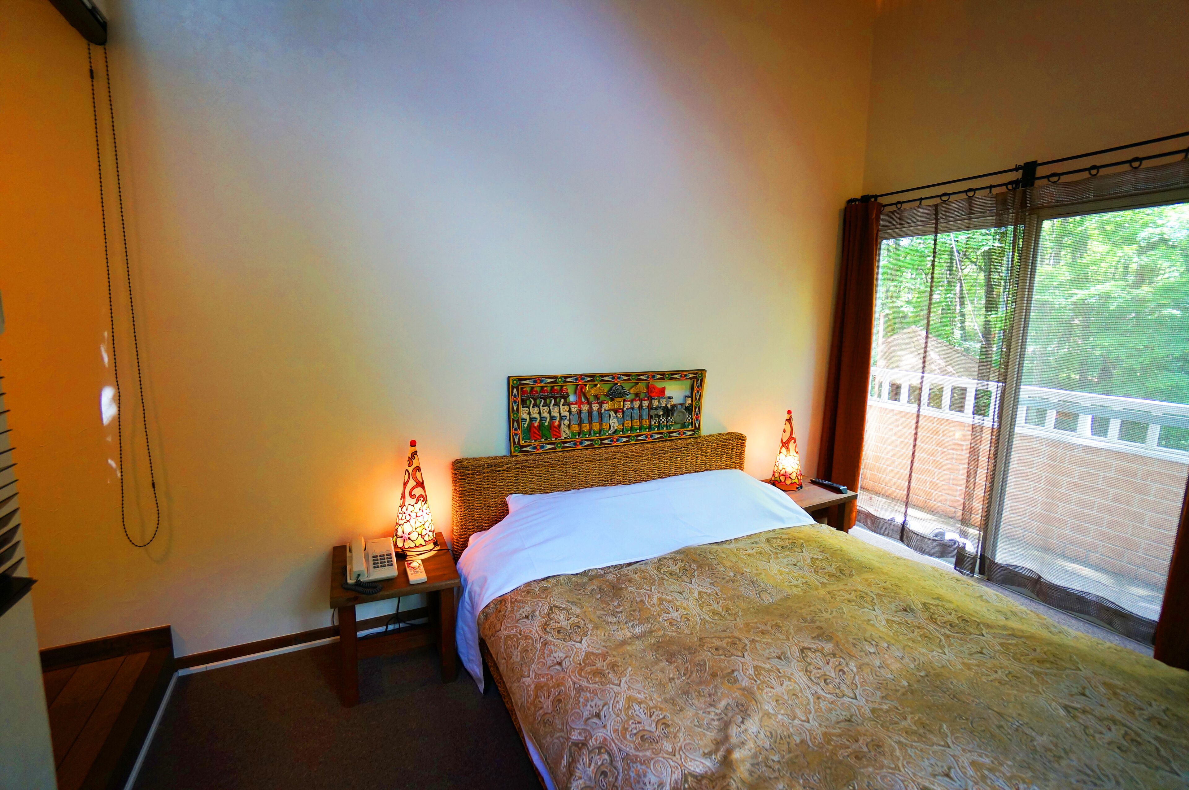 Quarto com uma cama grande, cabeceira decorativa, mesa de cabeceira com abajur e janela com vista para o exterior.