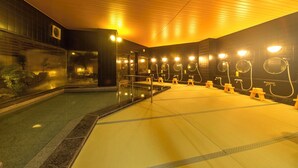 Uma onsen japonesa tradicional com várias áreas de banho, uma área de observação com paredes de vidro e teto de madeira.
